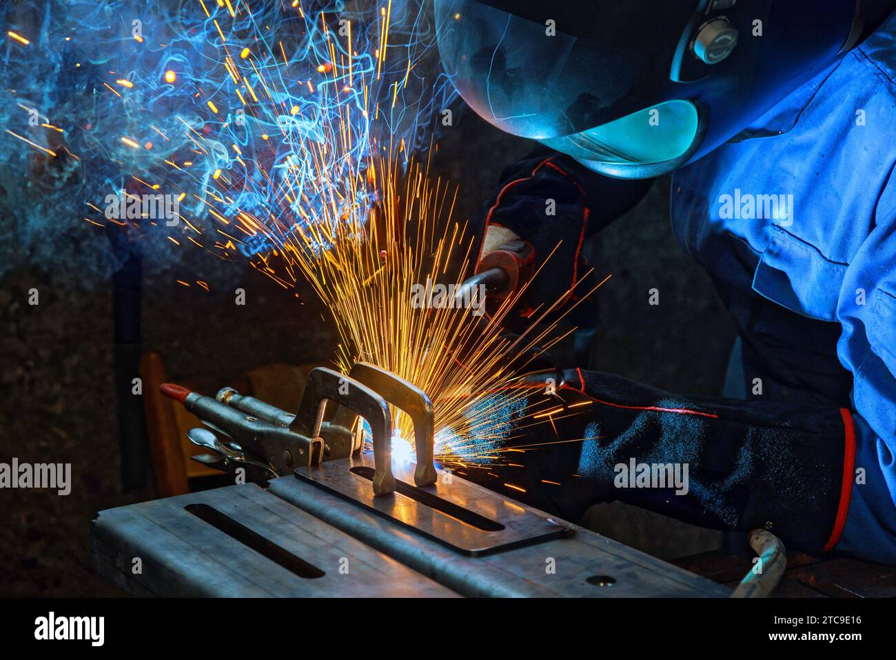 As worker welds steel with gas argon, sparks are generated that smoke ...