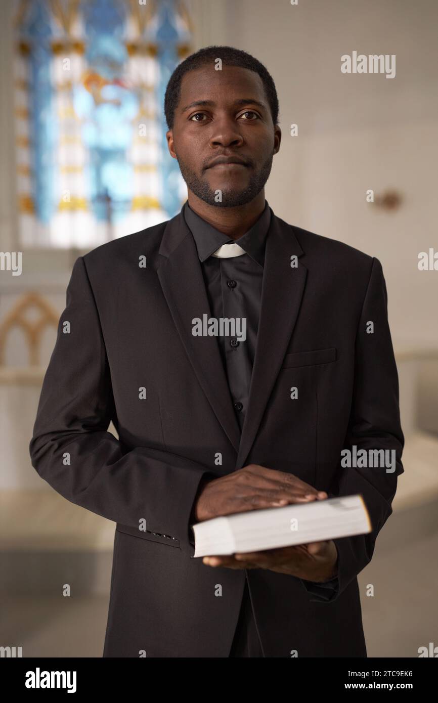 Vertical waist up portrait of Black young man as priest holding Bible ...