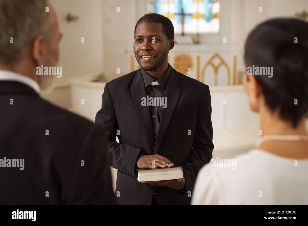 Waist up portrait of smiling Black young man as priest officiating ...