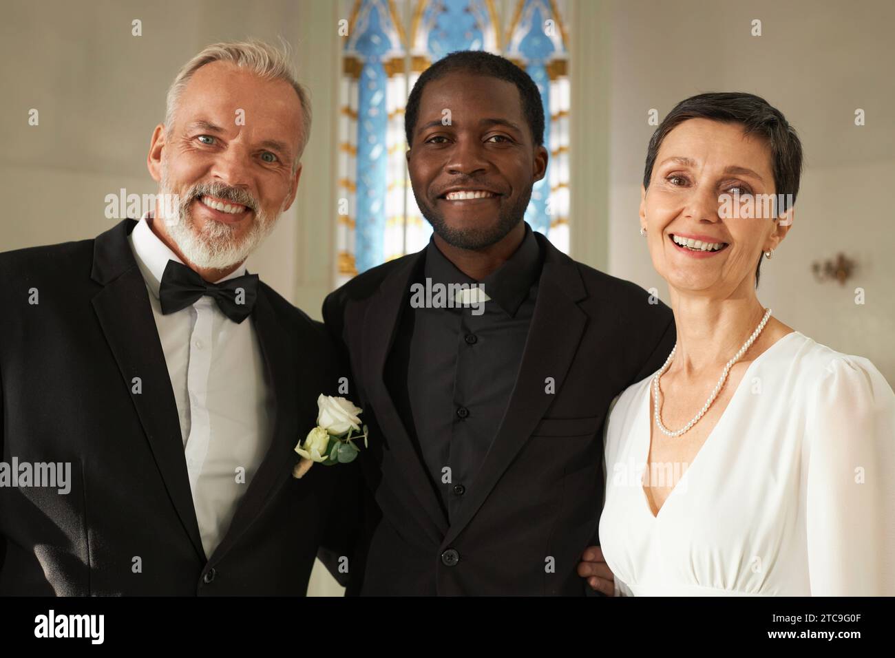 Waist up portrait of newlywed senior couple posing with smiling priest ...