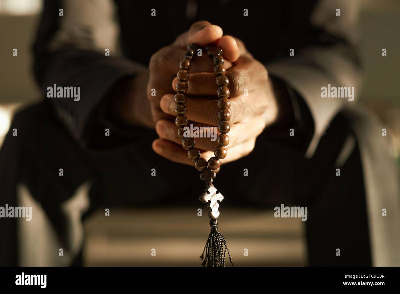 Closeup of priest holding wooden rosary beads and praying in ethereal ...