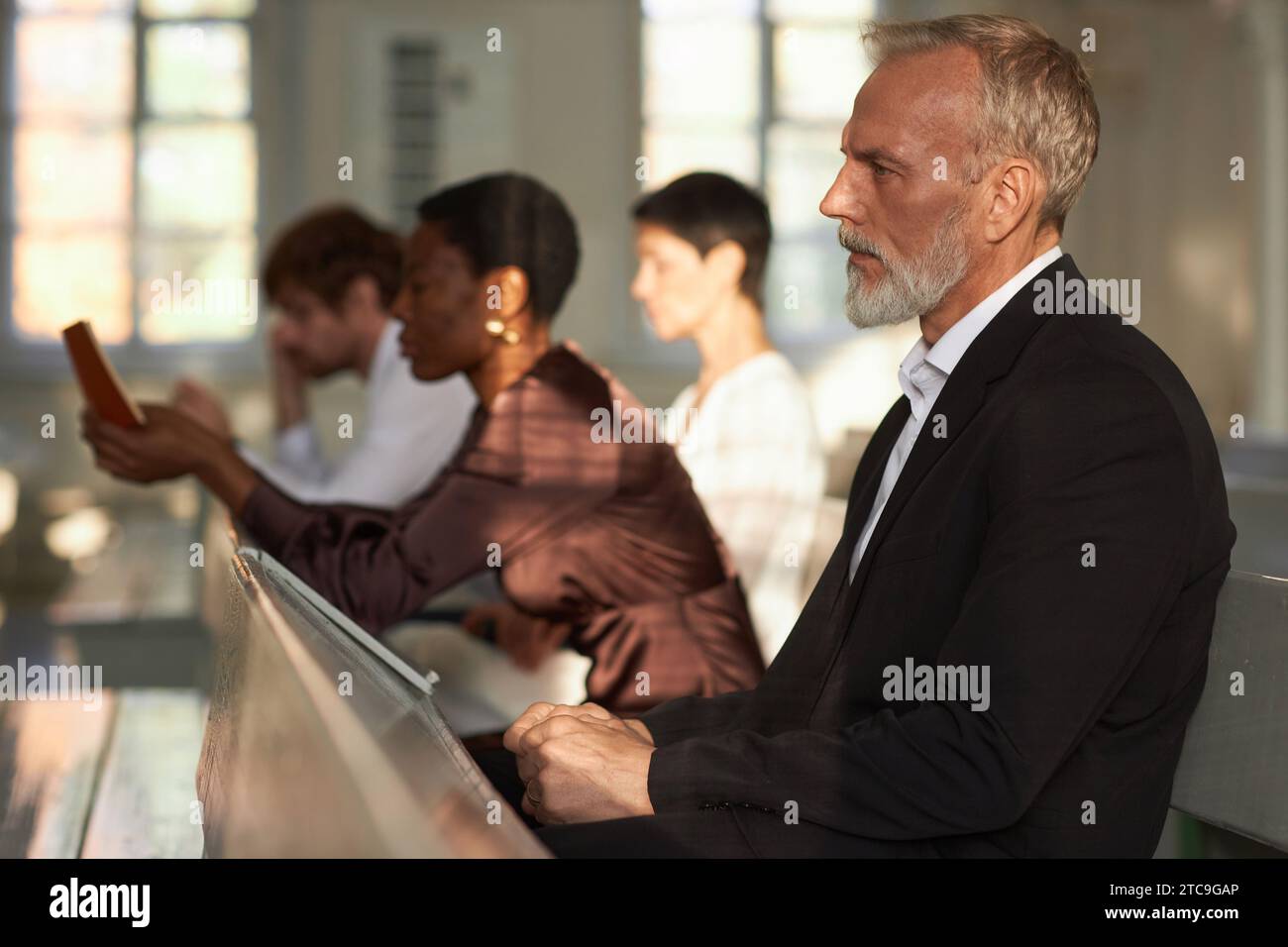 Side view portrait of bearded senior man sitting in pew at church and ...