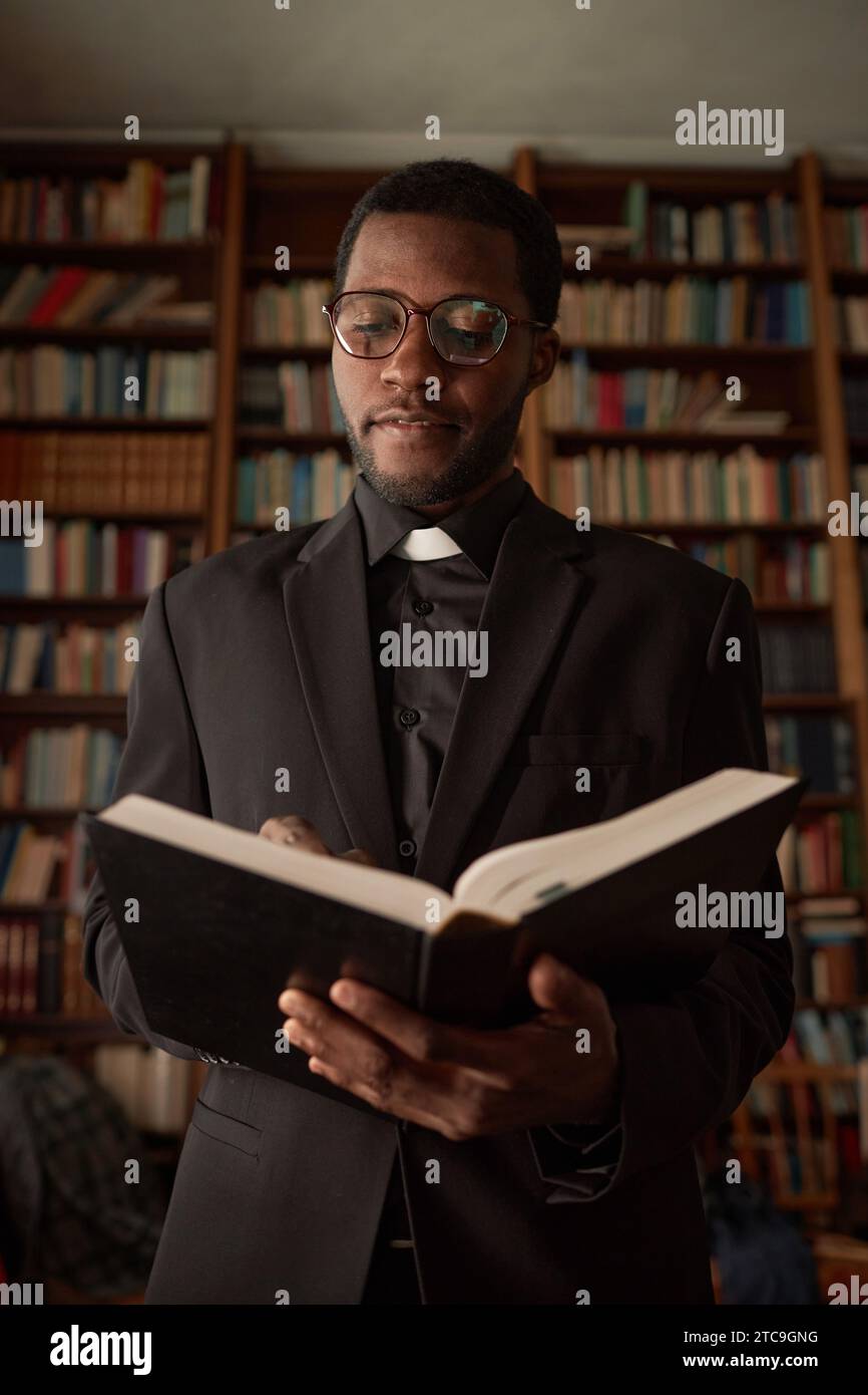 Vertical portrait of young African American man as priest reading Bible ...