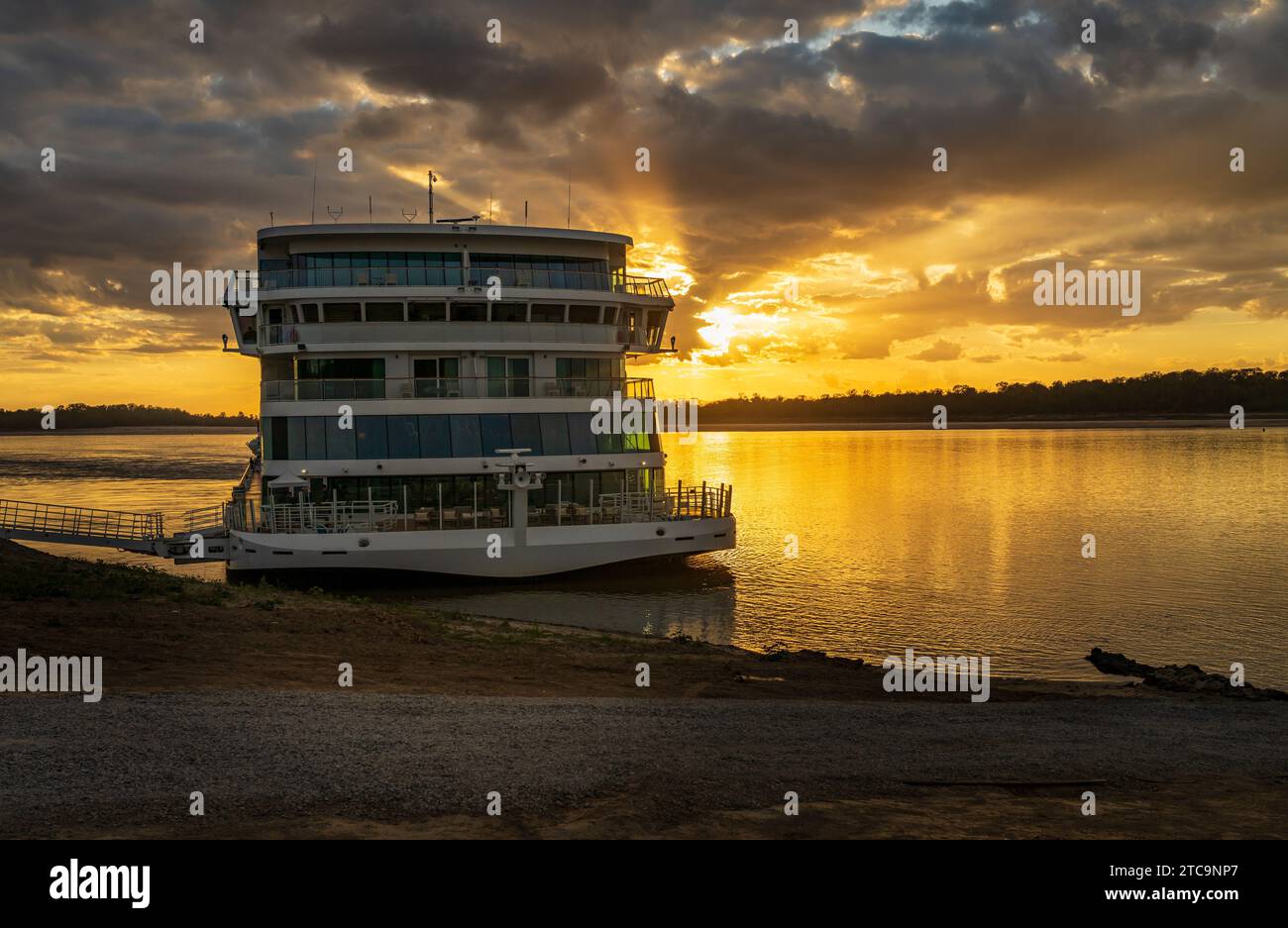 Bow of modern river boat docked by bank as sunset cast golden glow on ...