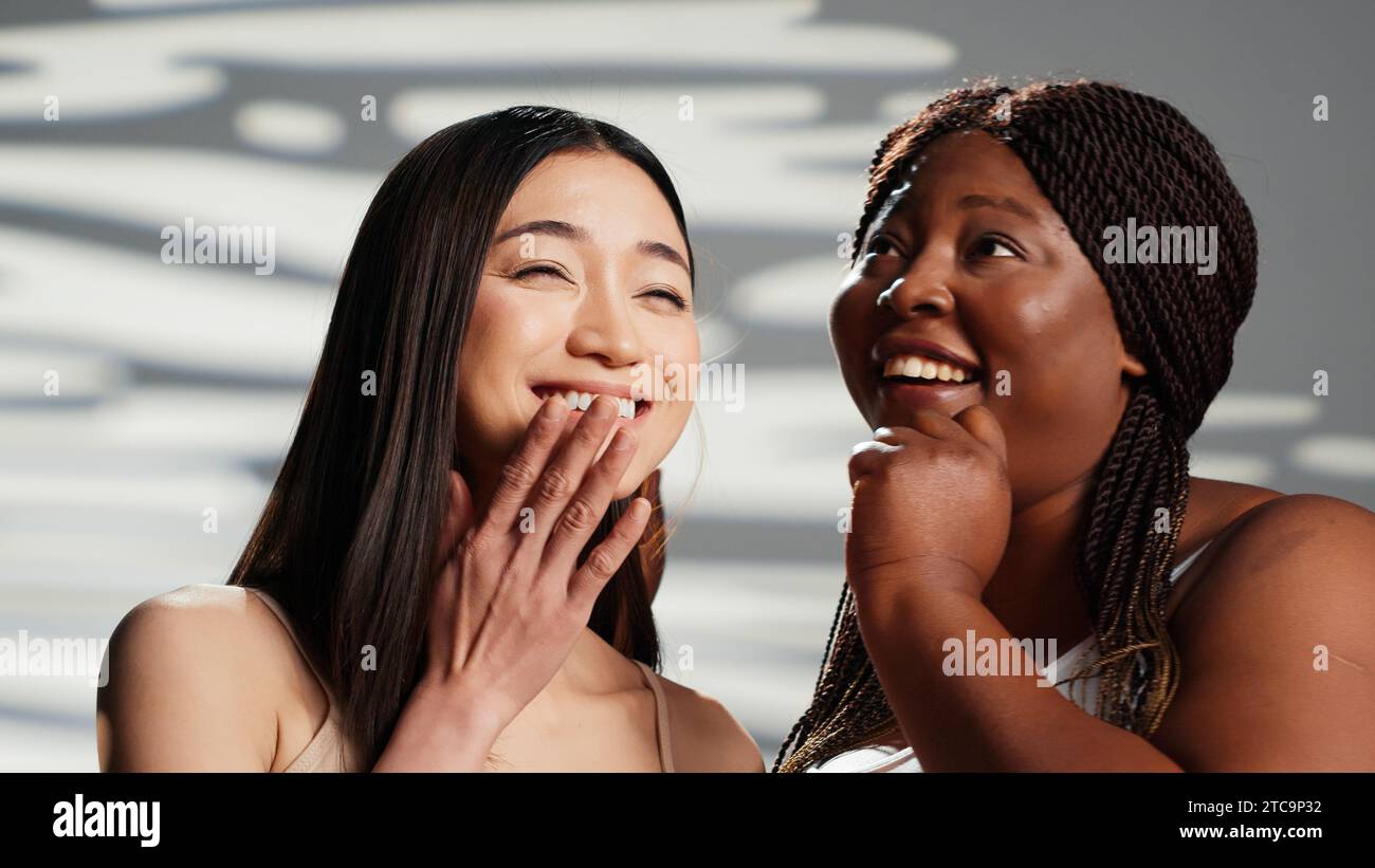 African american woman sharing secret with asian girl, creating ...