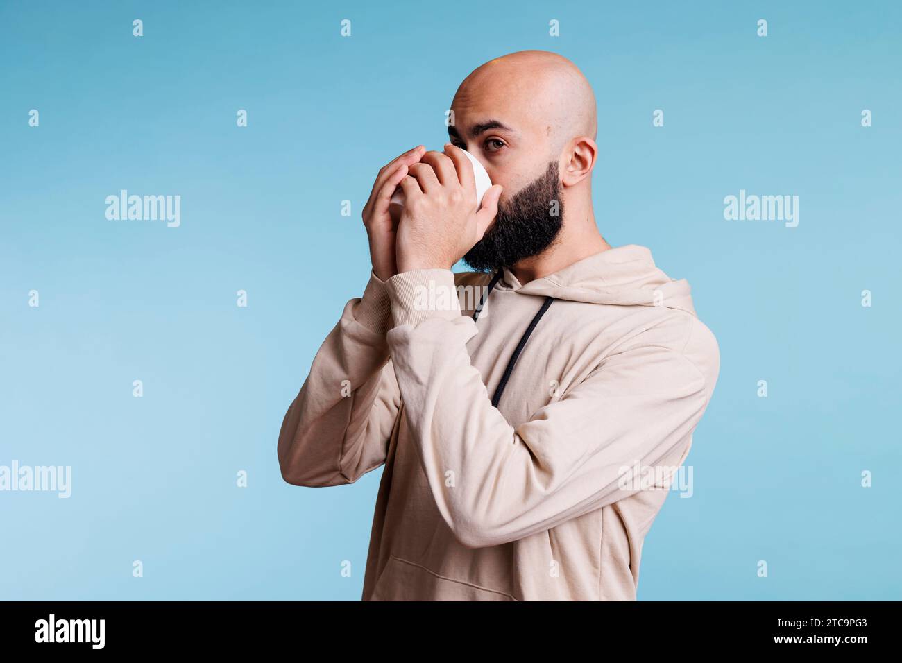 Young bald arab man enjoying morning cup of tea with relaxed facial ...