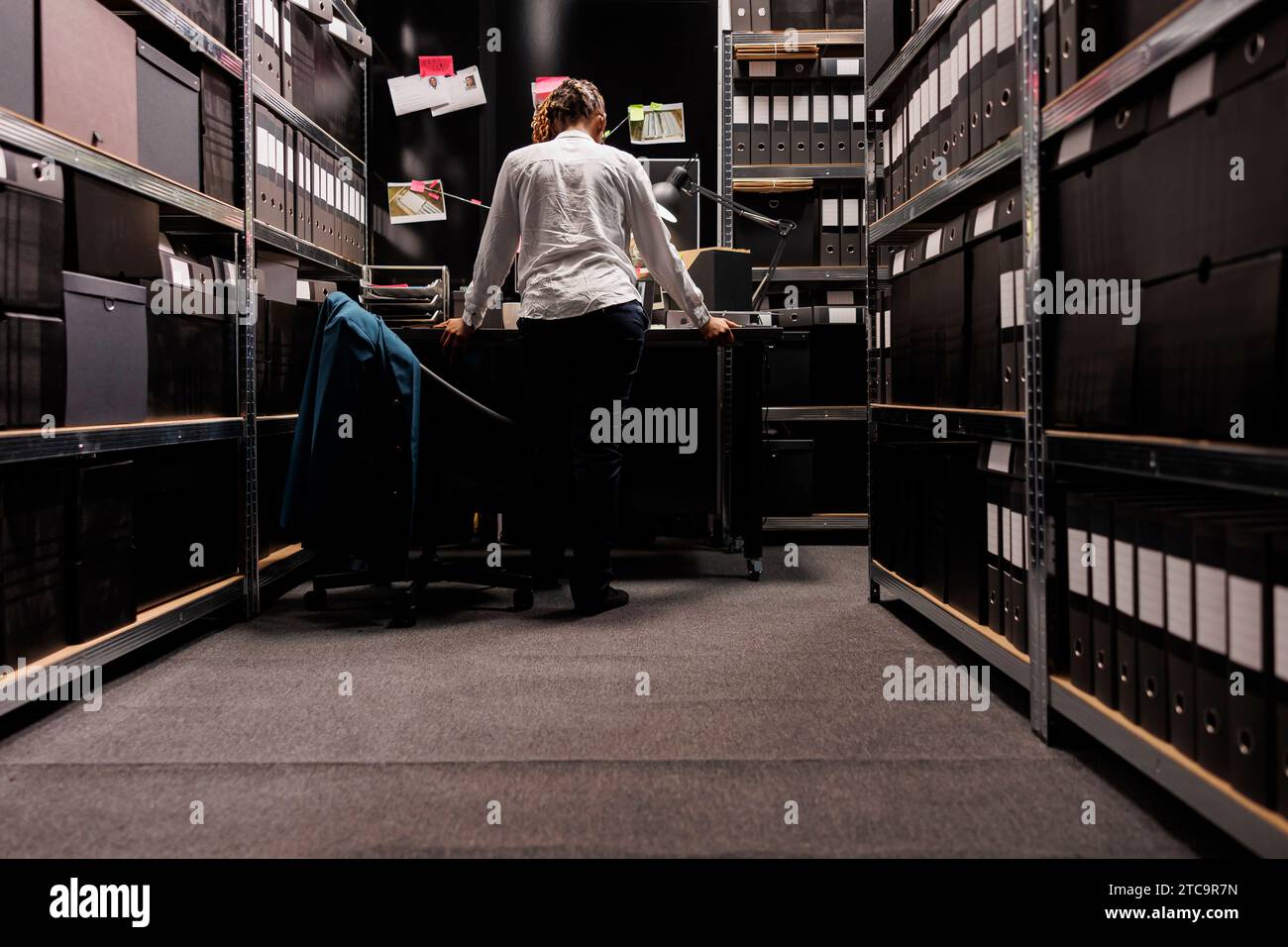 Police detective standing near desk and analyzing clues board in dark ...
