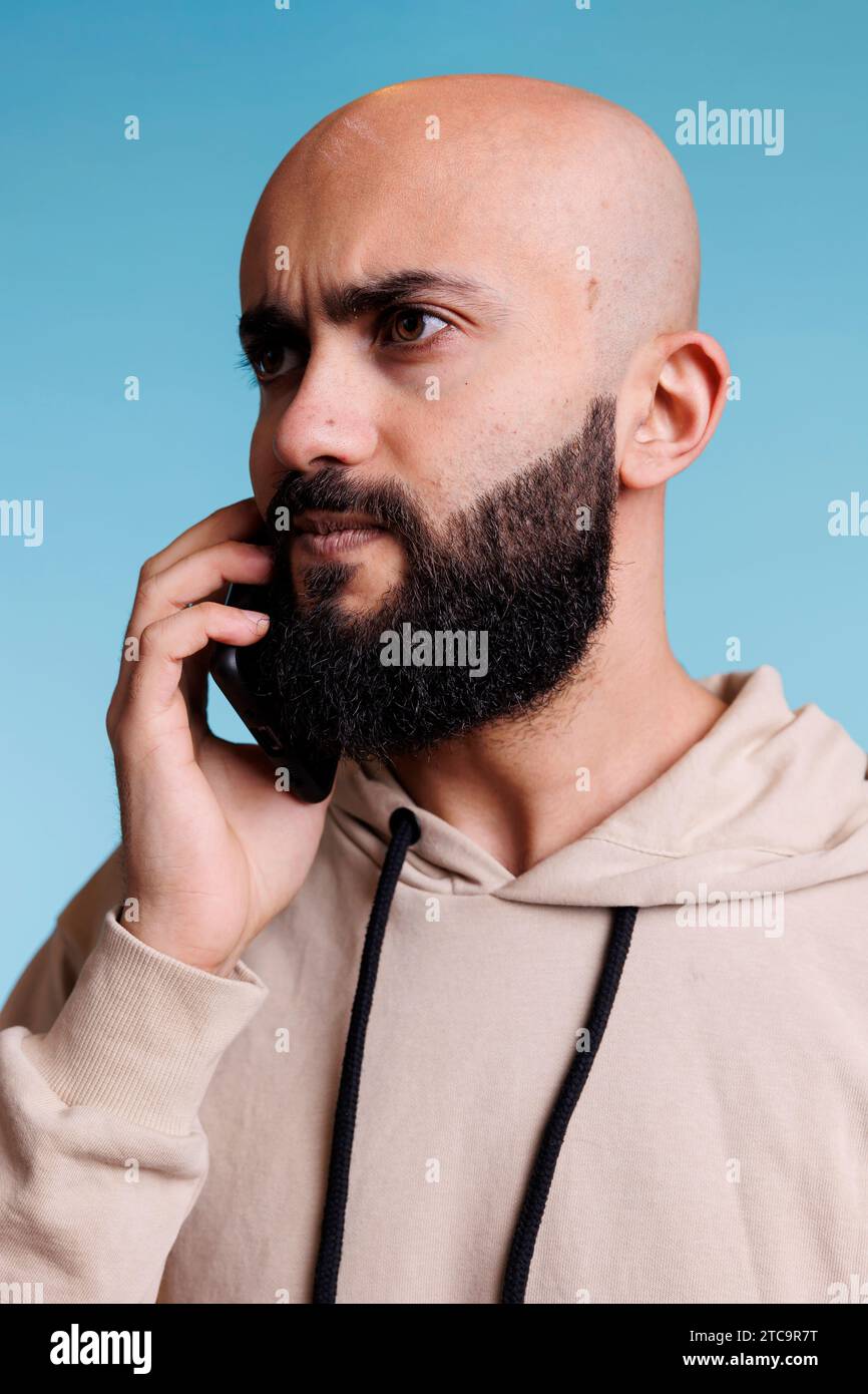 Serious arab man talking on smartphone and looking away. Young bald ...