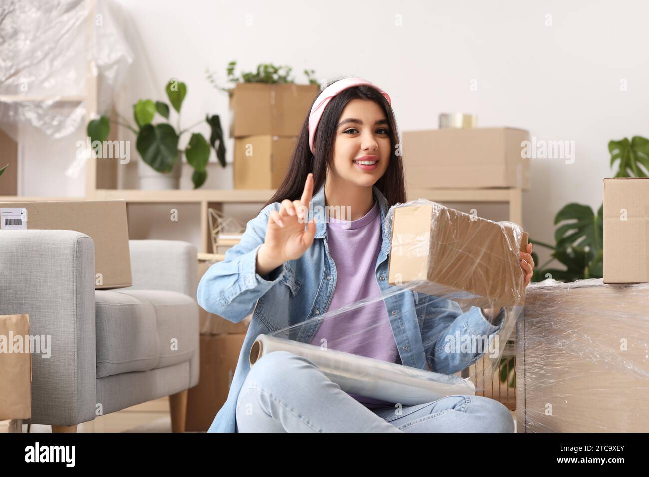 Young woman wrapping cardboard box with stretch film at home on moving ...