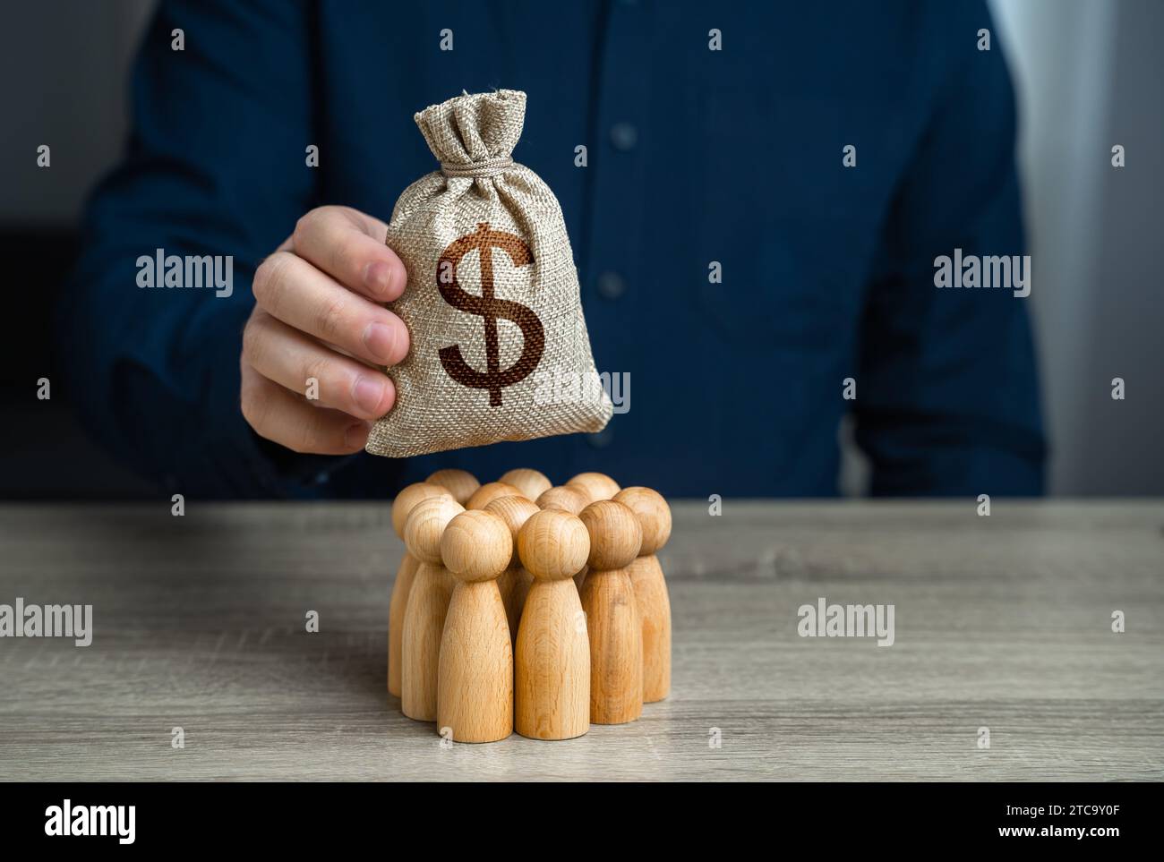 A man is holding a dollar money bag over a group of people figurines ...