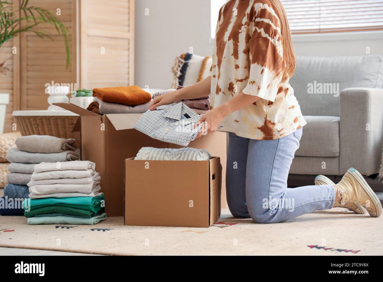 Young woman packing clothes into cardboard box in living room Stock ...