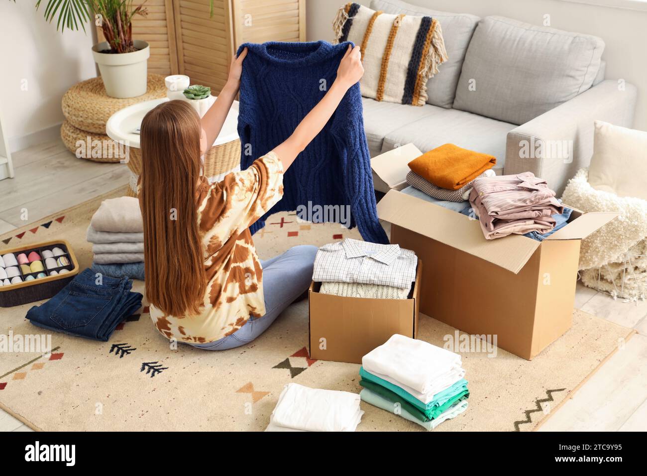Young woman packing clothes into cardboard box in living room Stock ...