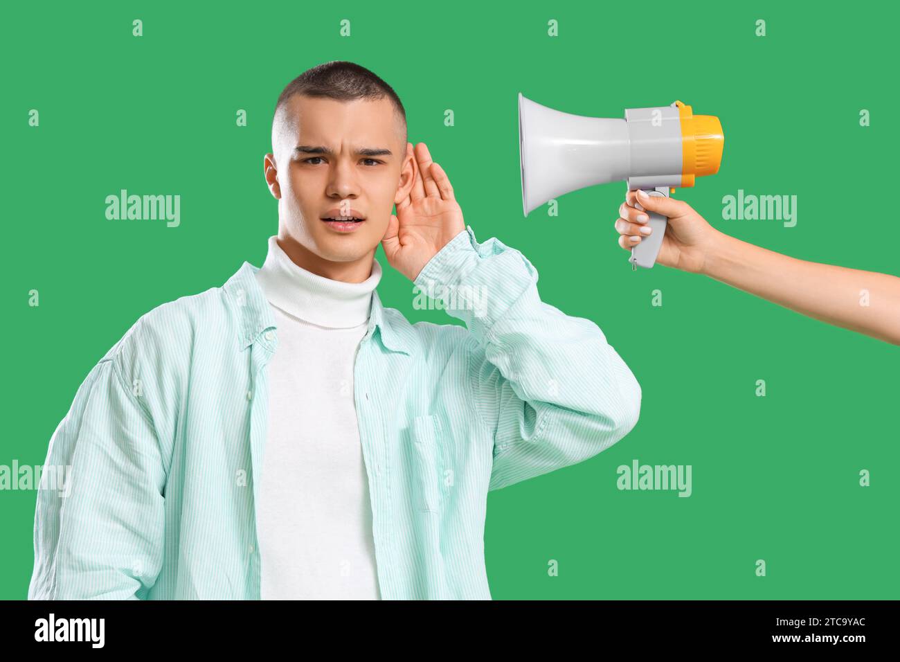 Teenage boy trying to hear something and hand with megaphone on green ...