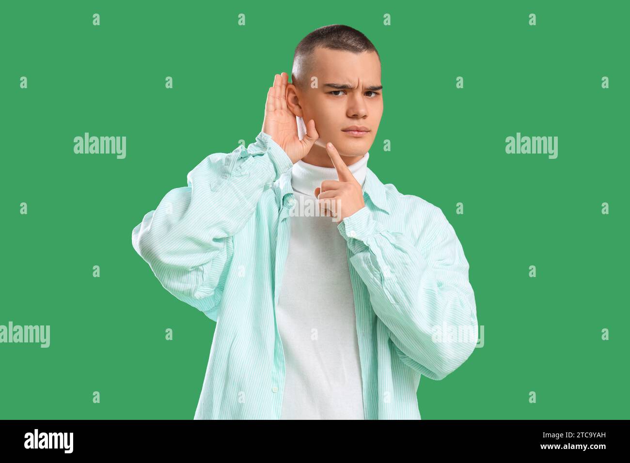 Teenage boy trying to hear something on green background Stock Photo ...