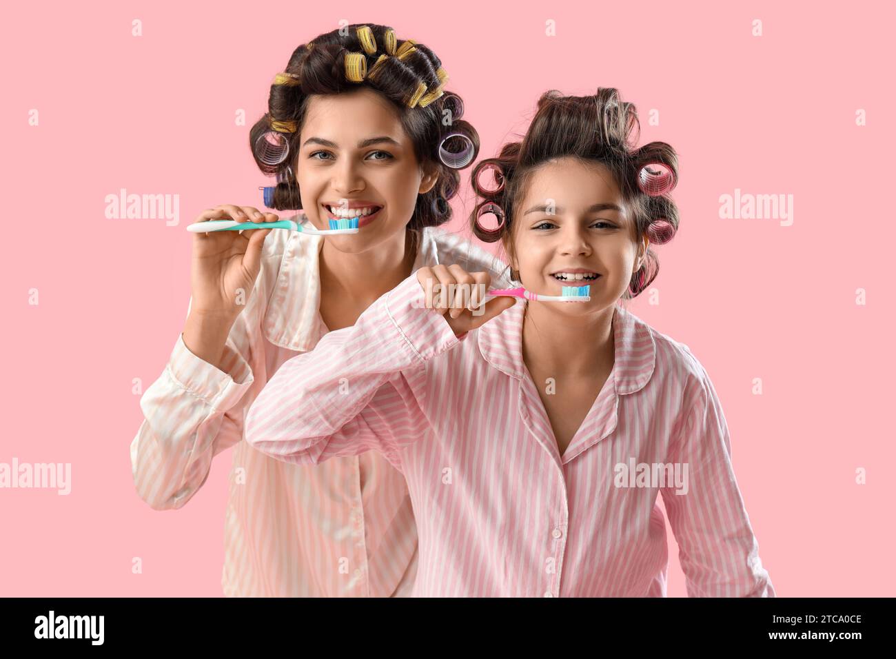 Little girl and her mother with hair curlers in pajamas brushing teeth ...