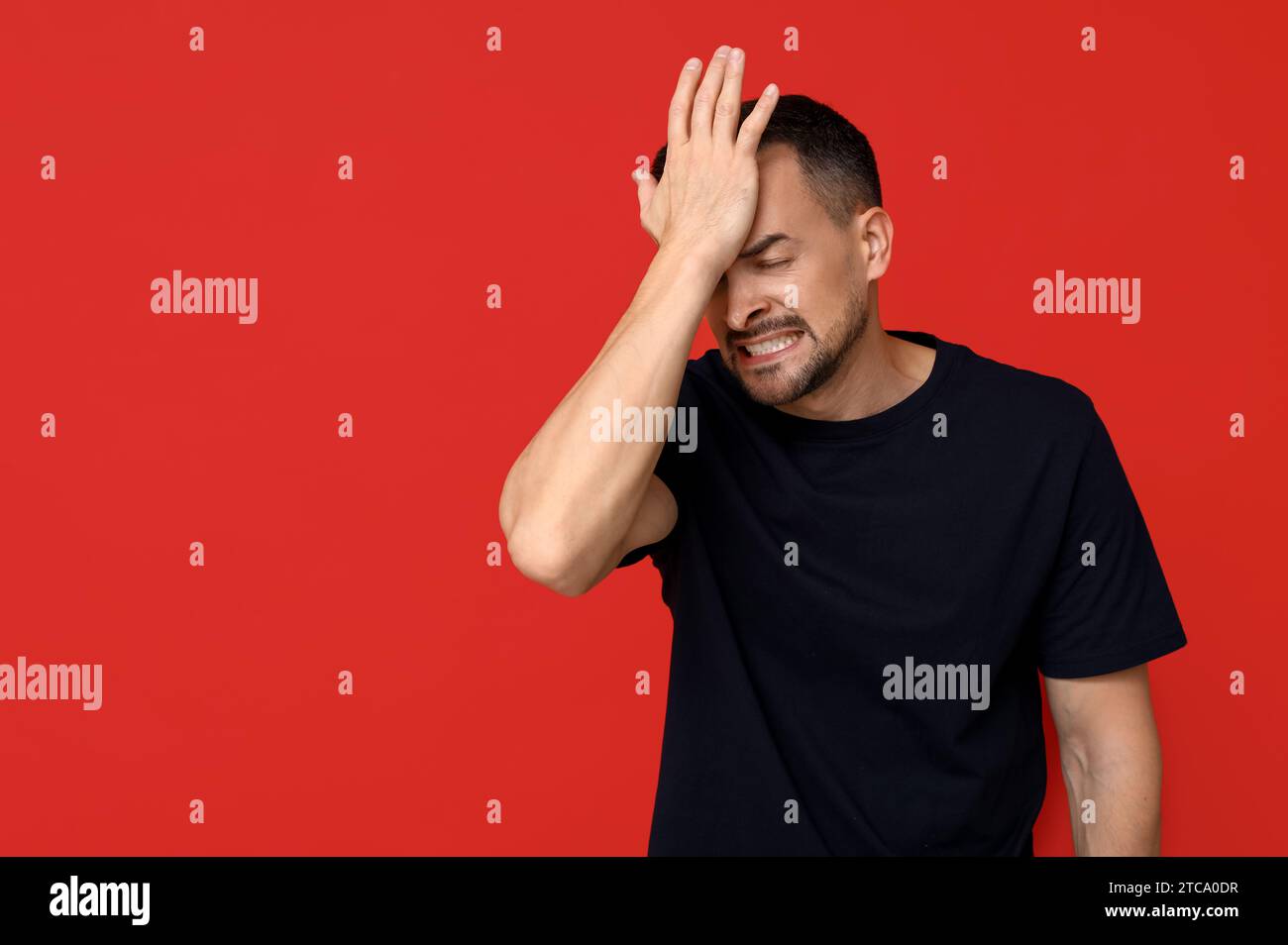 Handsome ashamed young man covering face with hand on red background ...