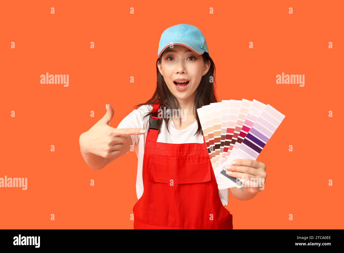 Female Asian shocked painter pointing at paint color palettes on orange ...