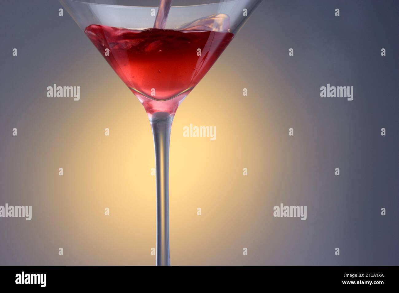 Pouring a Cosmopolitan mixed drink into stemware on a plain background ...