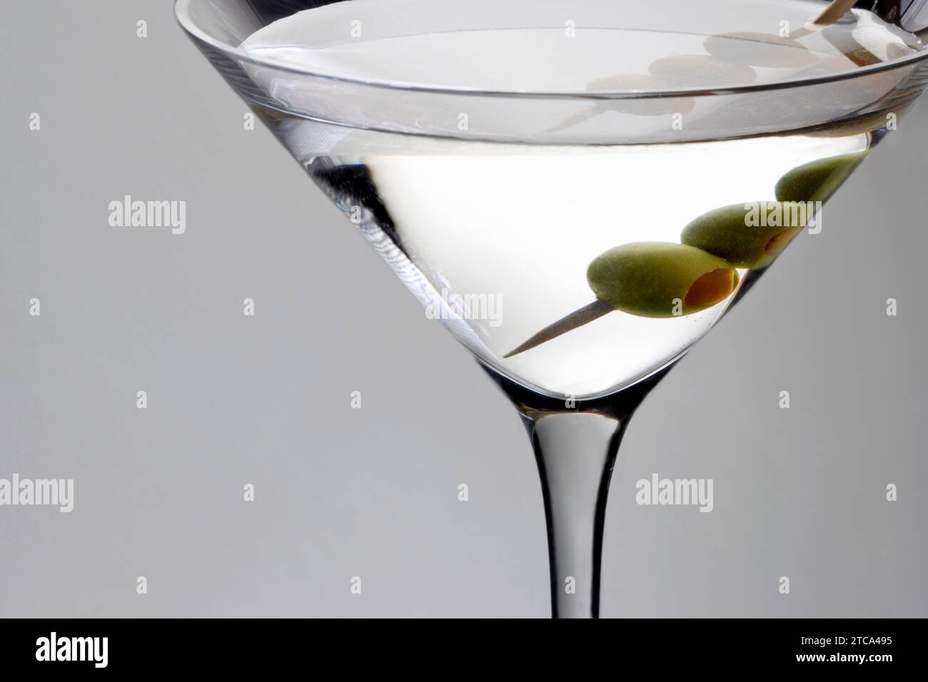 Martini mixed drink with olive garnish on a light grey background with ...