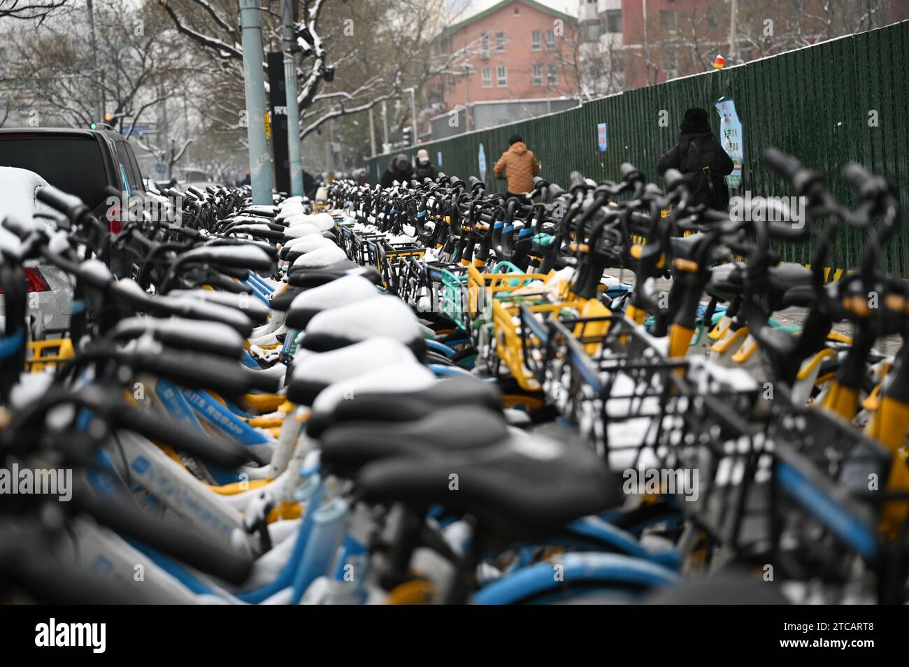 Peking, China. 12th Dec, 2023. Two people walk past parked rental bikes ...