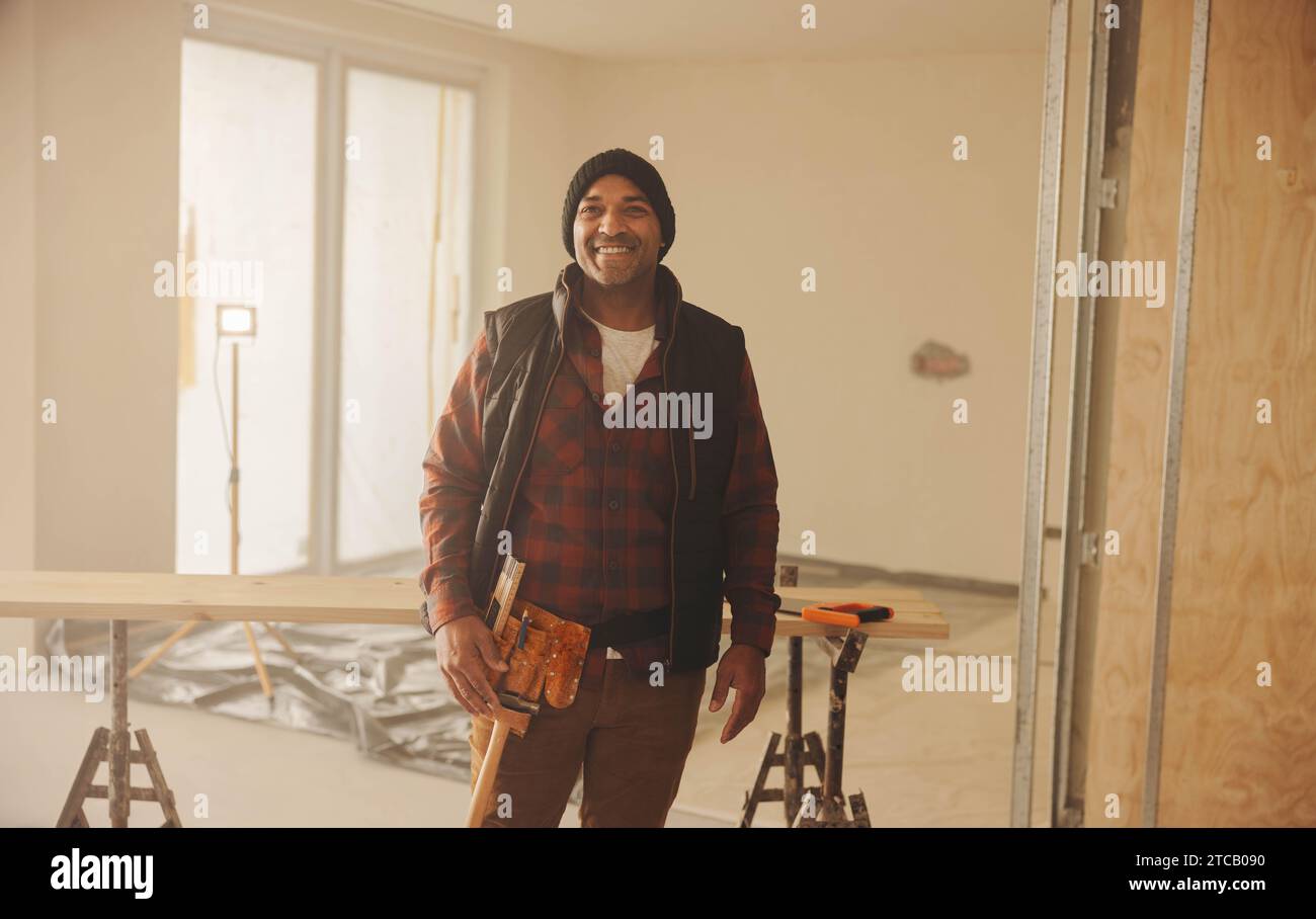 Mature male construction worker with a smile, standing in a kitchen. He ...