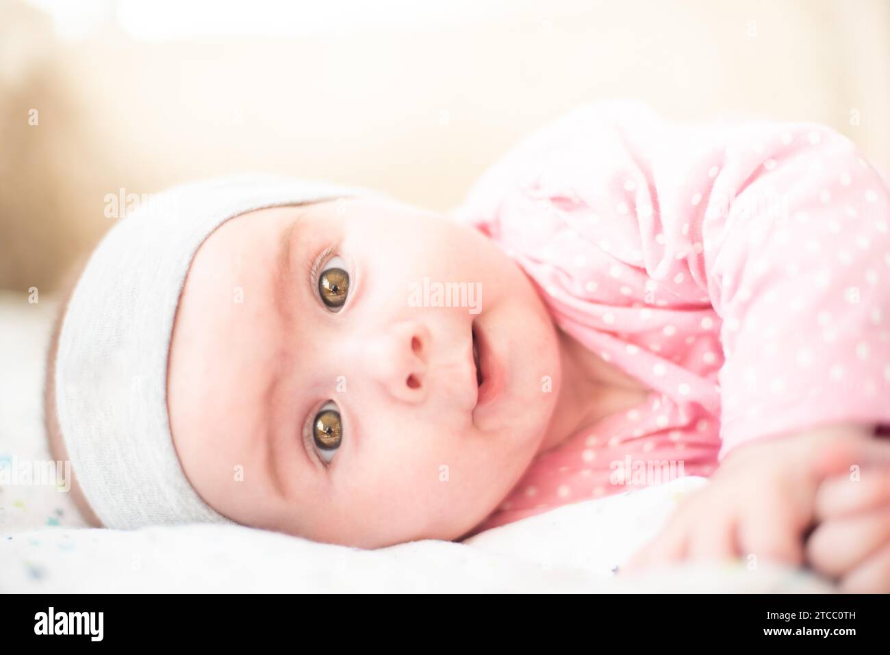 Adorable baby girl in pink lie on side and looking towards camera and smiling. Copy space on top ...