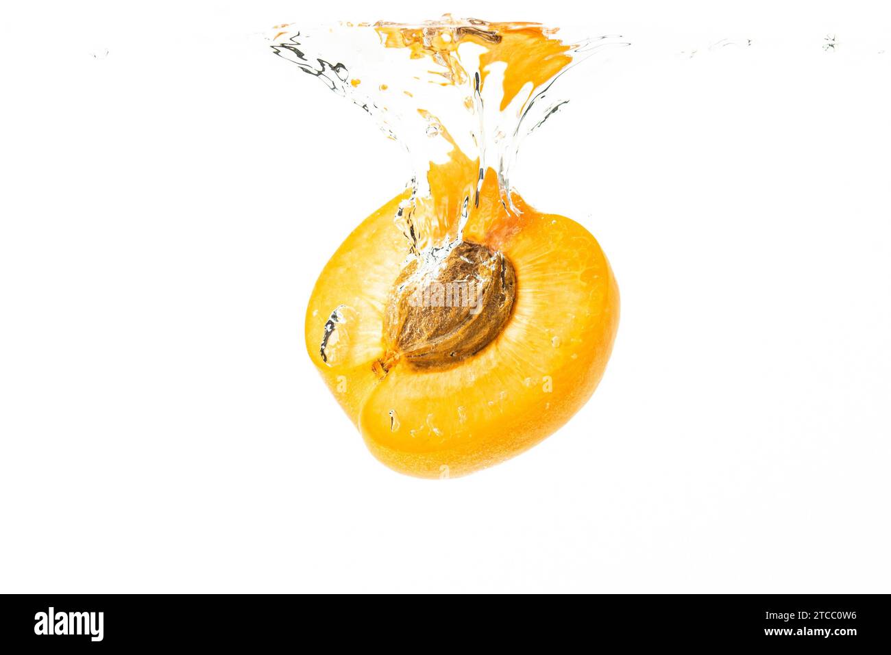 Fresh ripe organic apricot split in half falling in the clear water ...