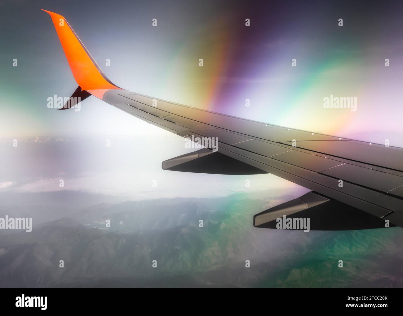 Wing of a civilian airliner in flight above clouds and mountains with ...