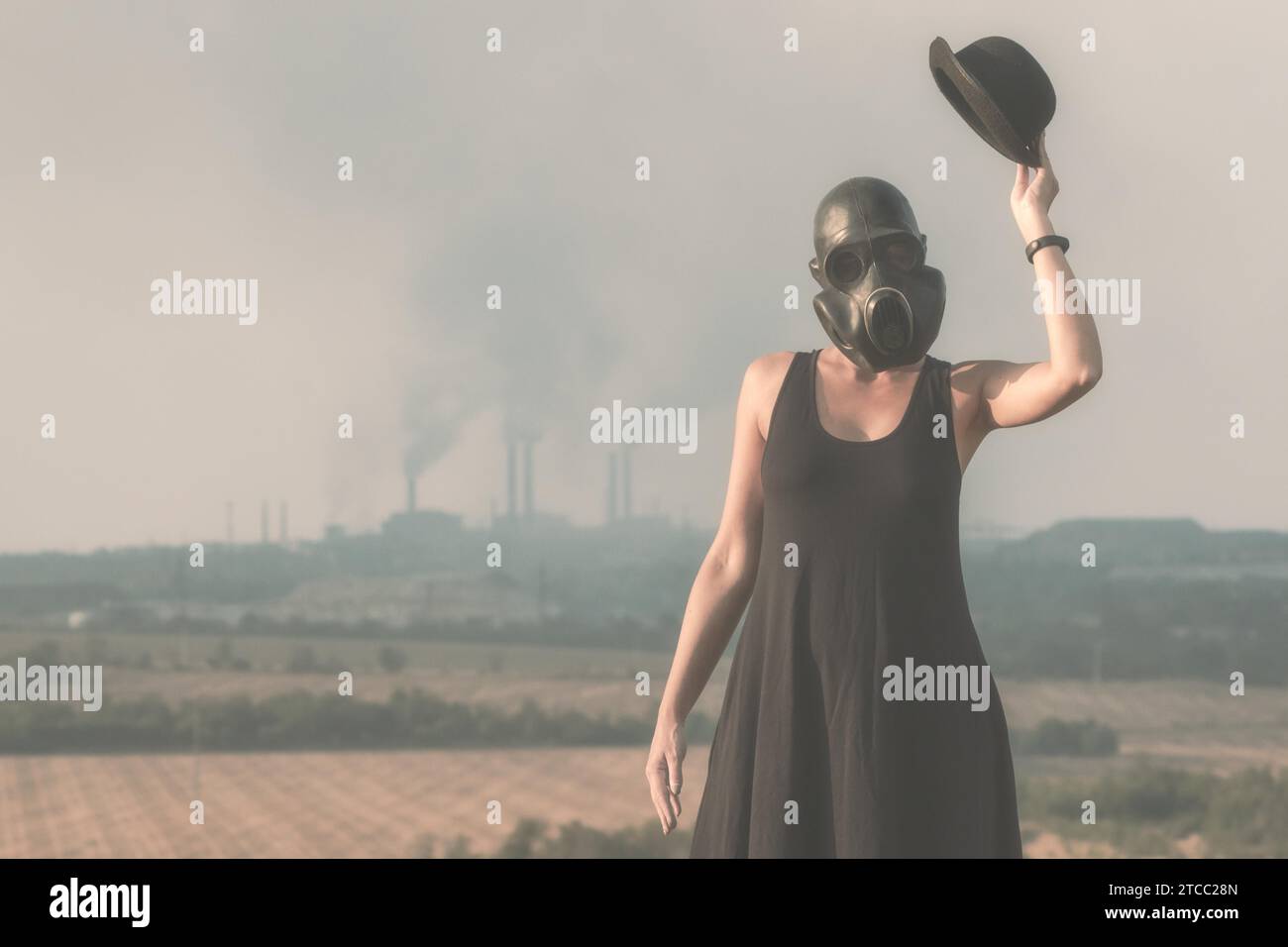 Young girl in a black dress and gas mask on the background of smoking ...
