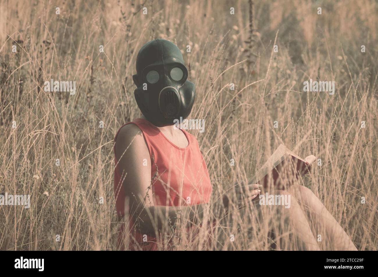 Young woman in gas mask in a red dress with a book in her hands sits in ...