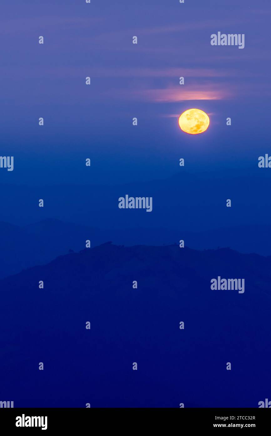 The full moon shines over blue mountains at dusk, the full moon against ...