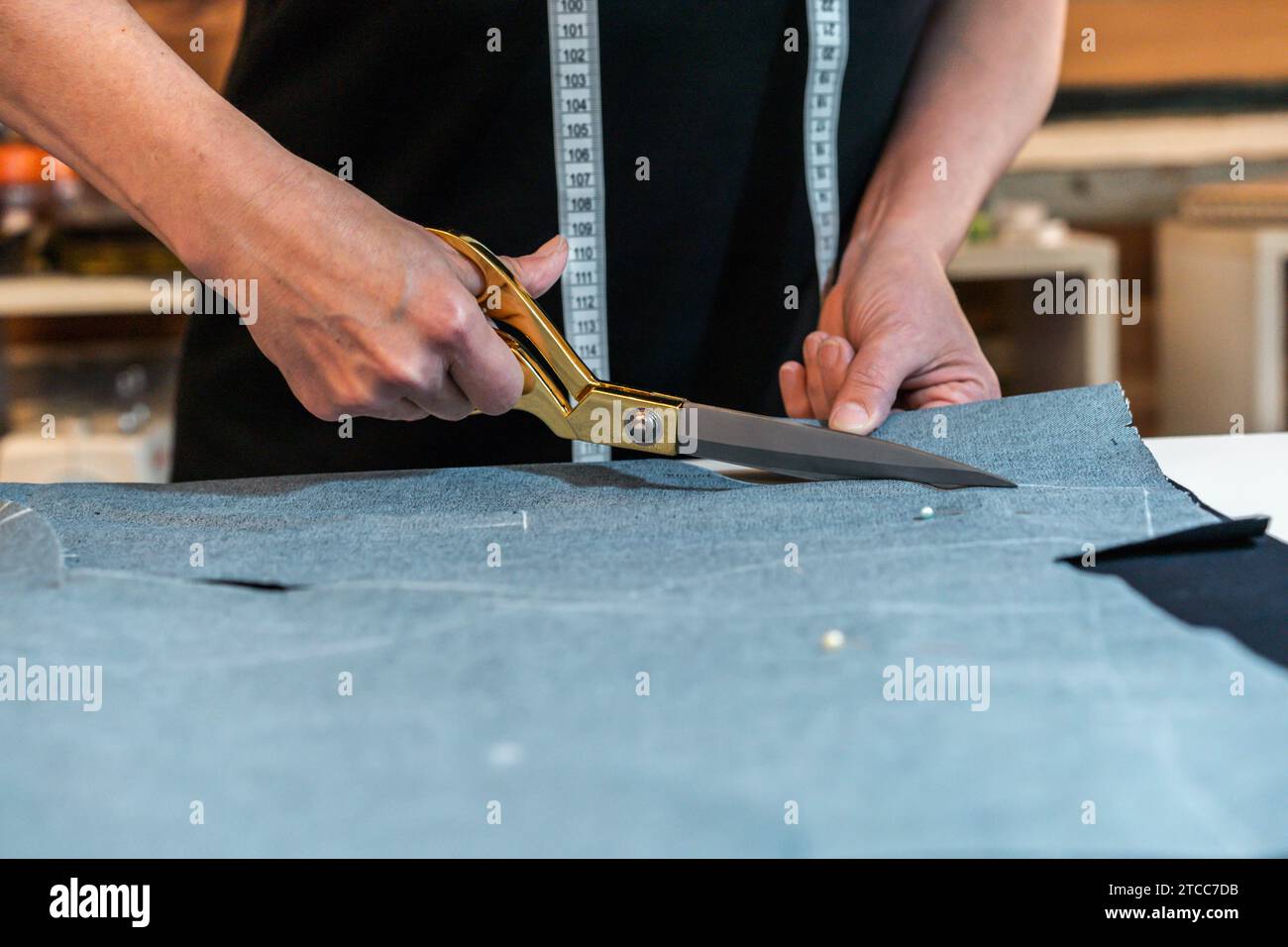 Seamstress using scissors to cut textile at work table Stock Photo - Alamy