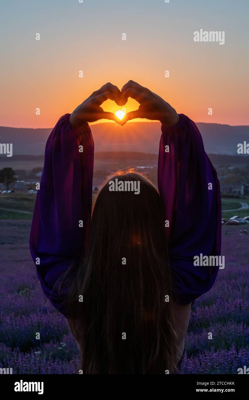 woman creates form a heart shape with hands at sunset. Conveying serene ...
