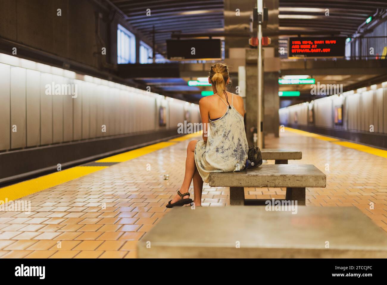 A woman alone sits on a bench and waits for a subway train in San ...
