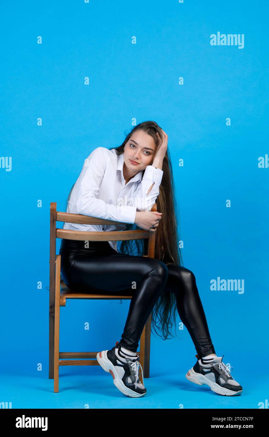 Young woman in stylish white blouse leaning on backwards chair back ...