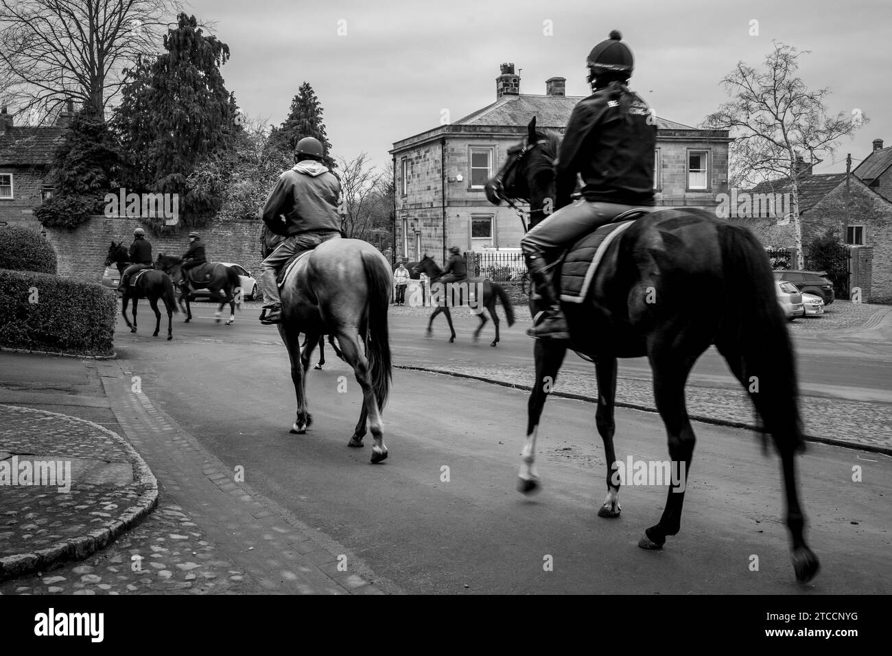 Black and white photo of men riding horses on a street, followed by ...