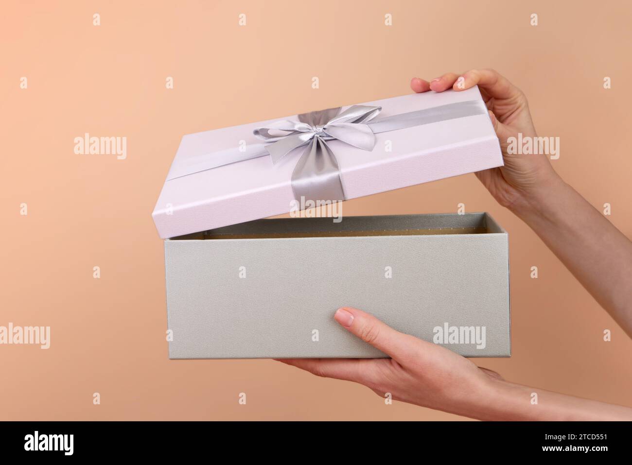 Side view of hands opening a box with a gift bow on a peach background ...