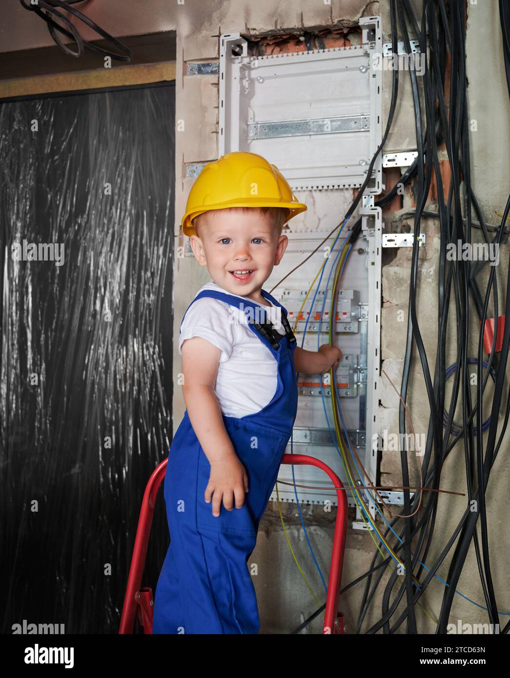 Happy little boy in construction safety helmet holding electrical wires ...