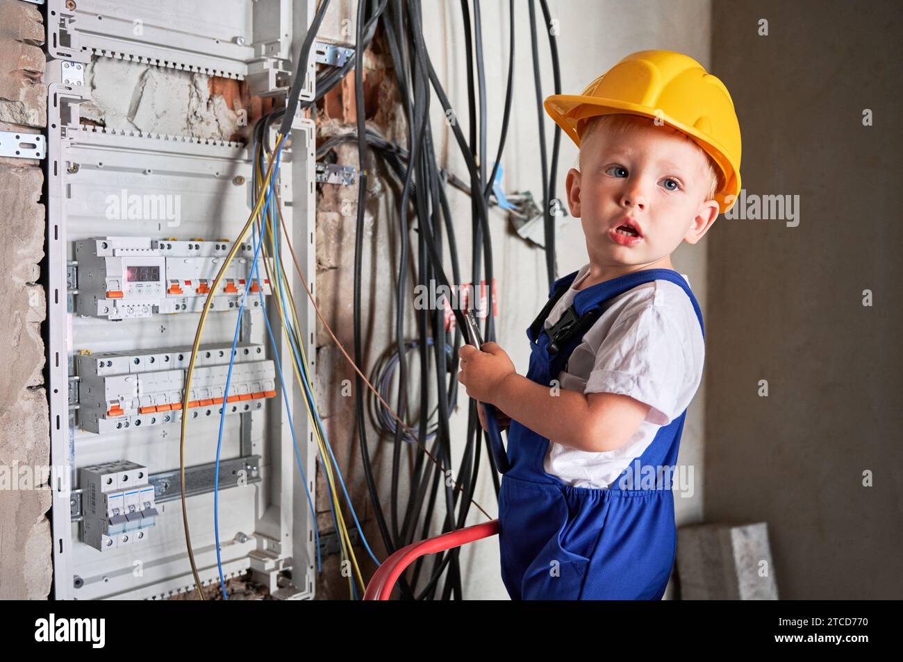 Portrait of child electrician cutting electrical wire with pliers while ...