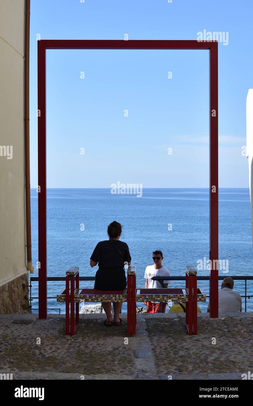 Women sitting on a bench underneath a large red rectangular art ...