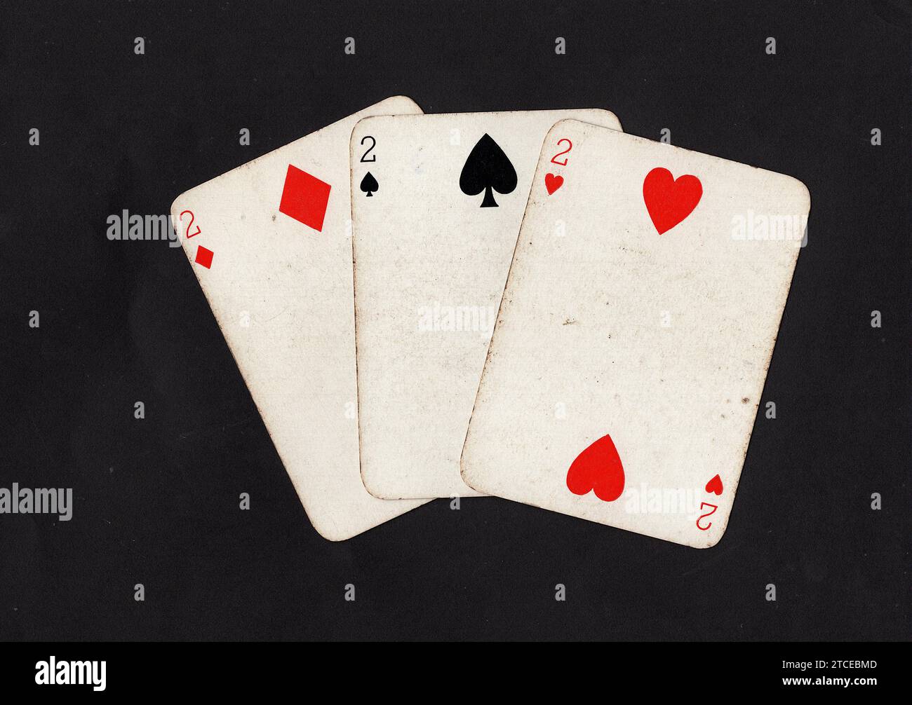 A hand of vintage playing cards showing three twos isolated on a black ...