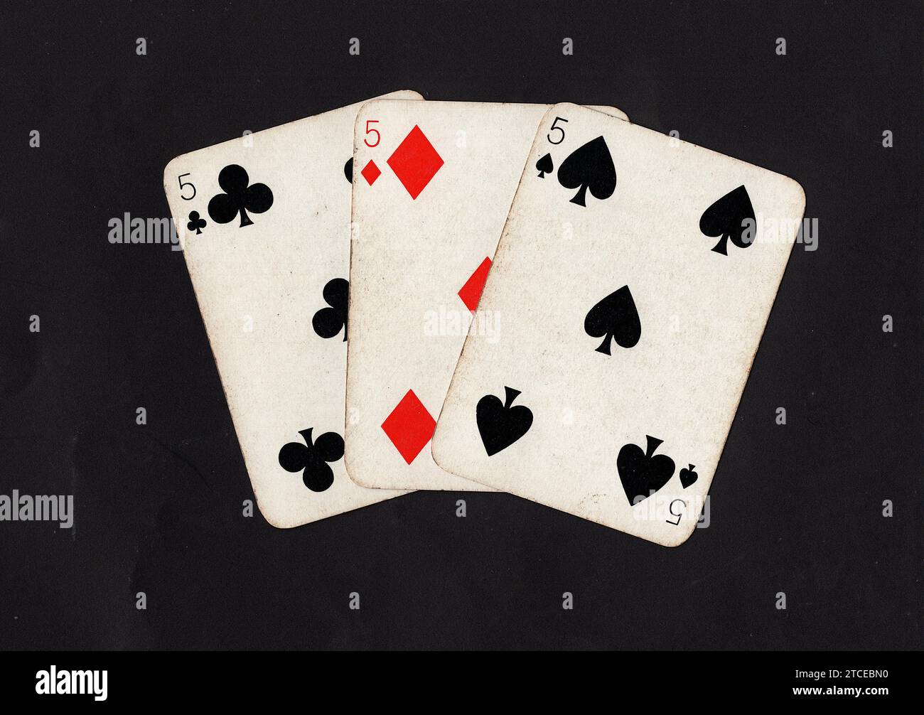 A hand of vintage playing cards showing three fives isolated on a black ...