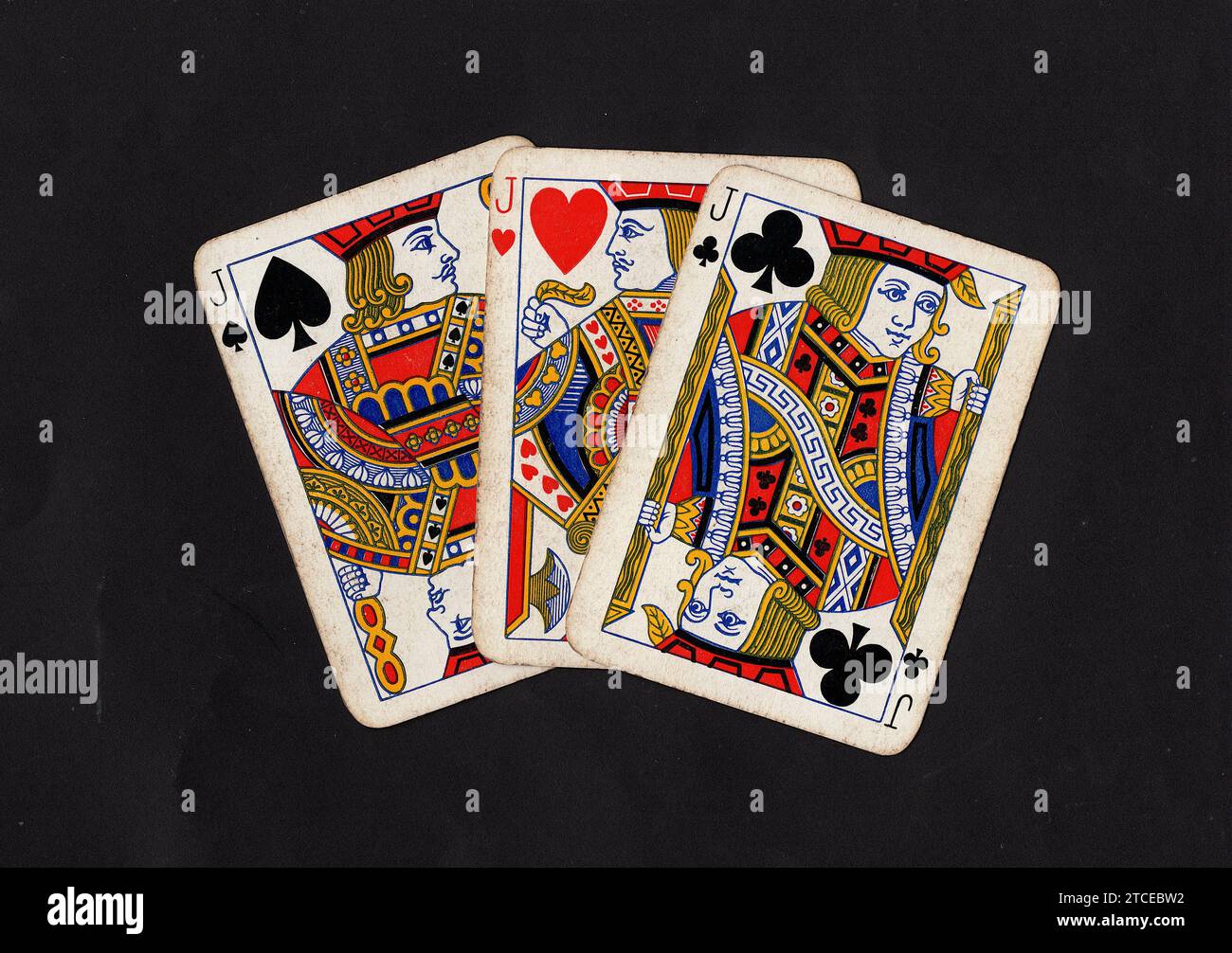 A hand of vintage playing cards showing three jacks isolated on a black ...