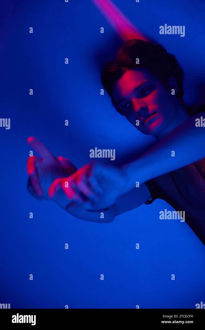 Young guy posing against dark blue background in neon light. Attractive ...