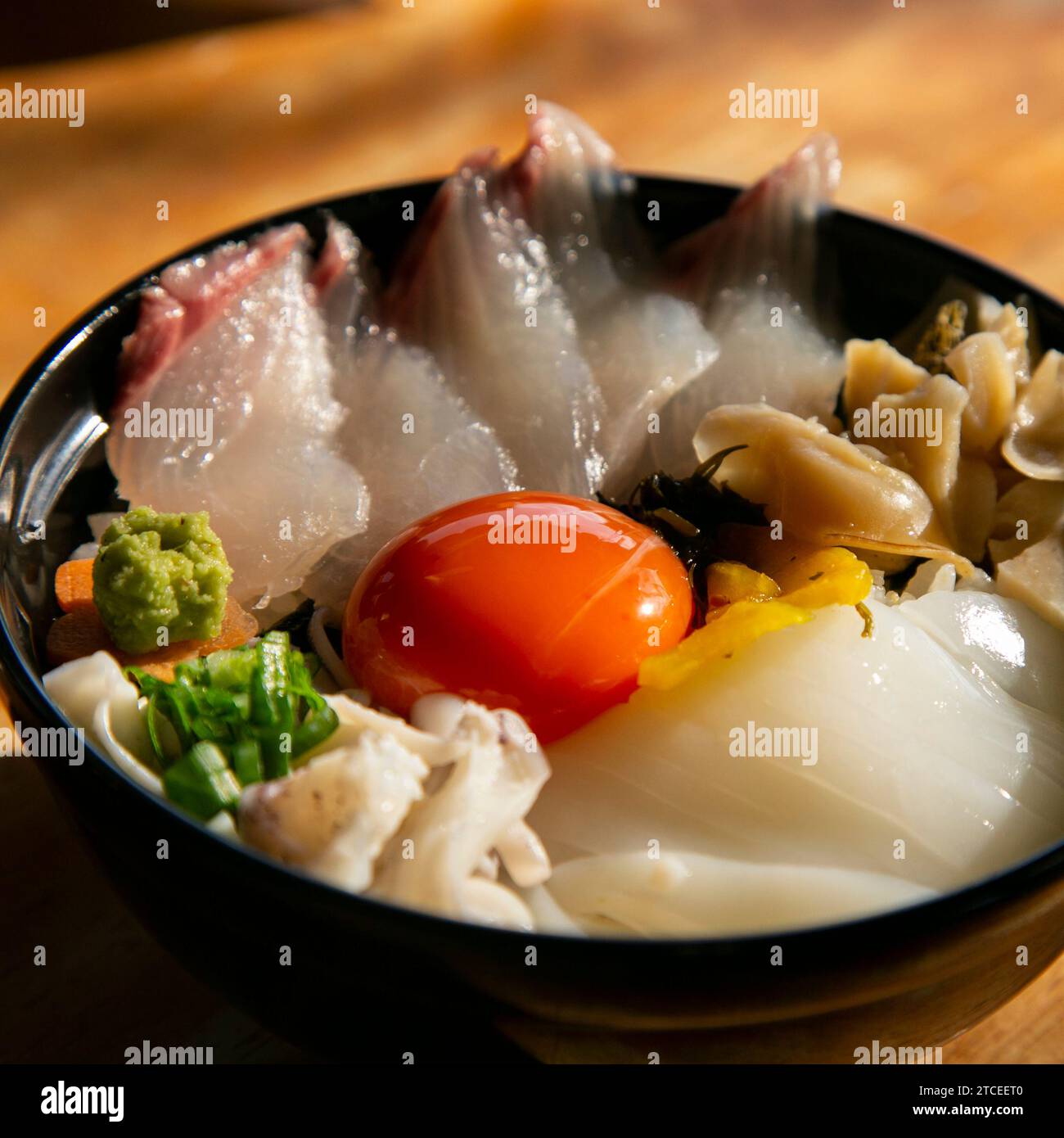 Japaneses sashimi donburi with white fish, squid and egg yolk on a bed ...