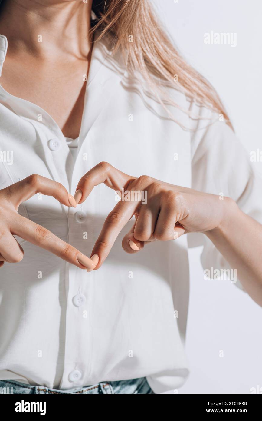 romantic young woman in shirt making a heart gesture with her fingers ...