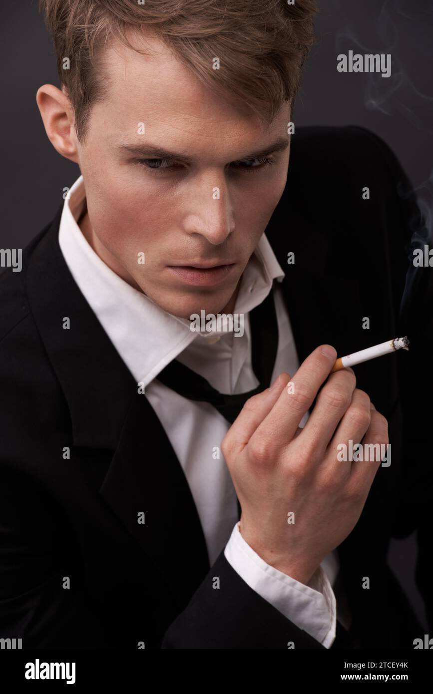 Face, thinking and a man smoking a cigarette in studio on a dark ...