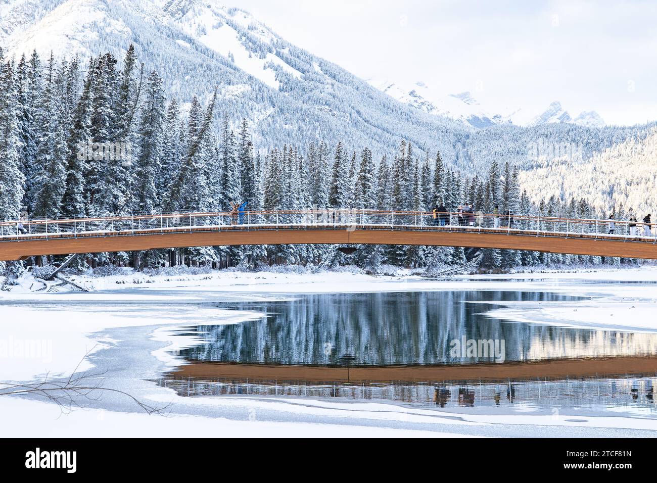 Pedestrian bridge in Banff over Bow River with reflections in winter ...