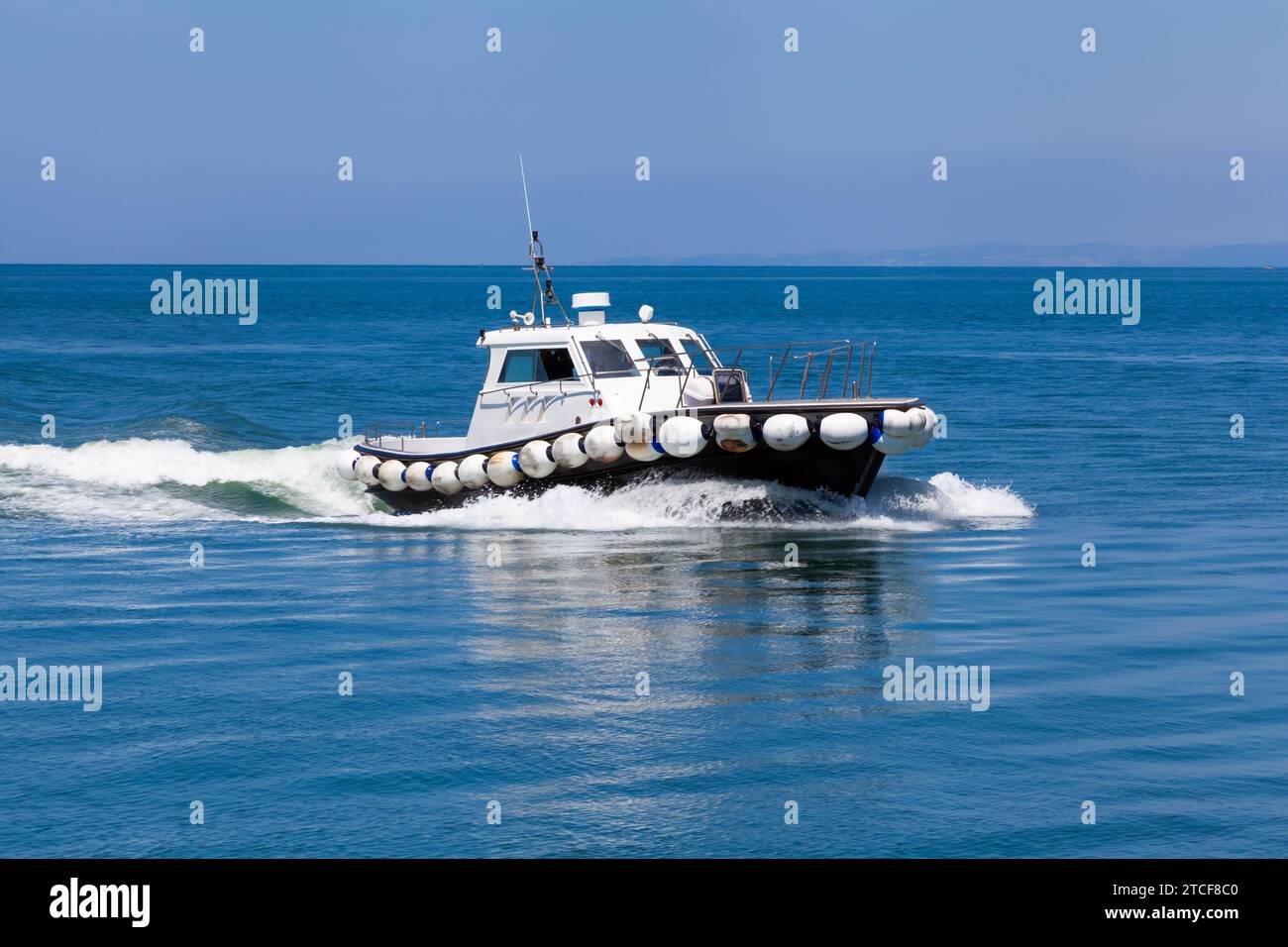 White boat with antenna, creating wake in calm blue waters, distant ...