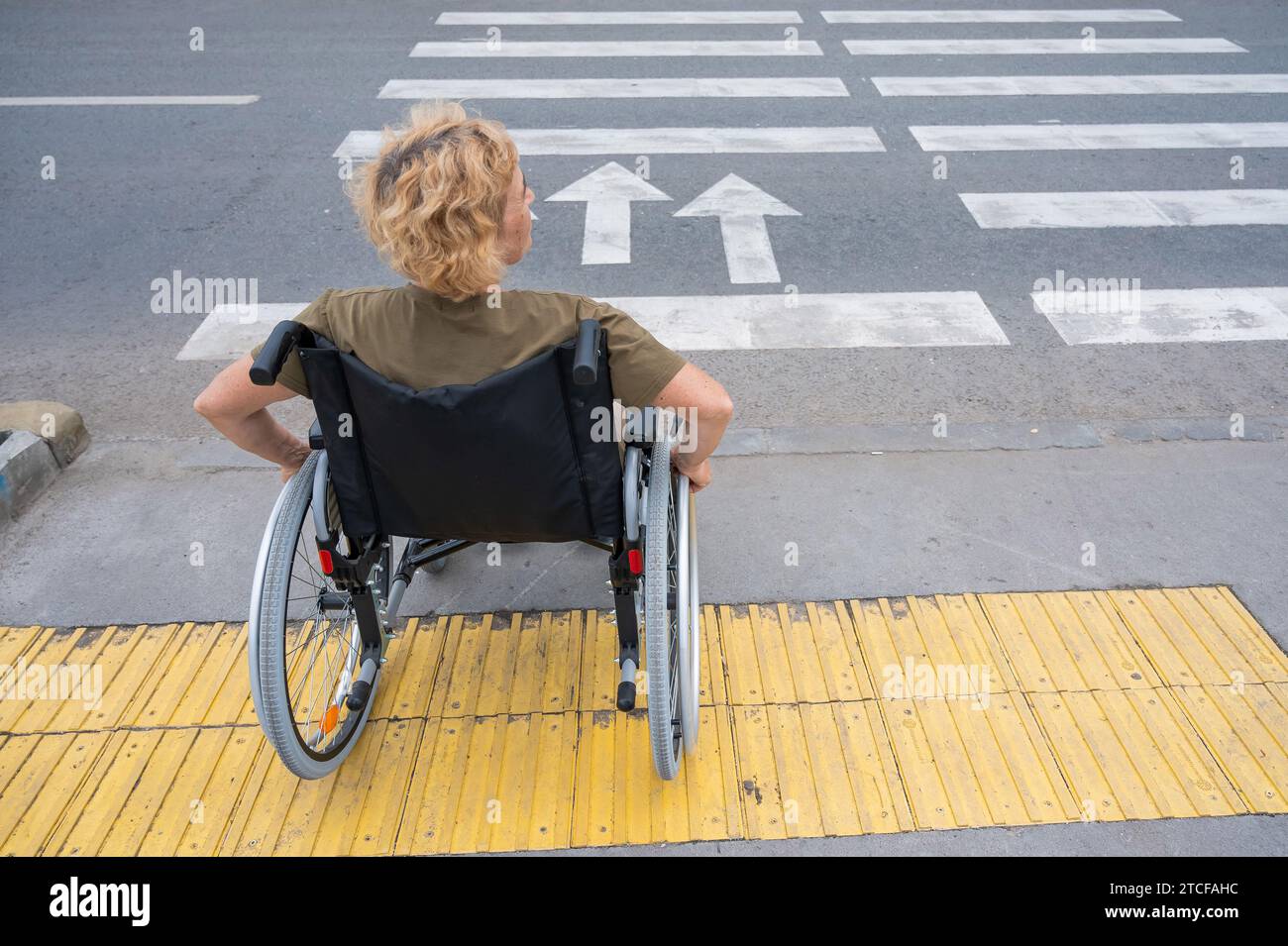 Rear view of an elderly woman on a wheelchair going to a pedestrian ...